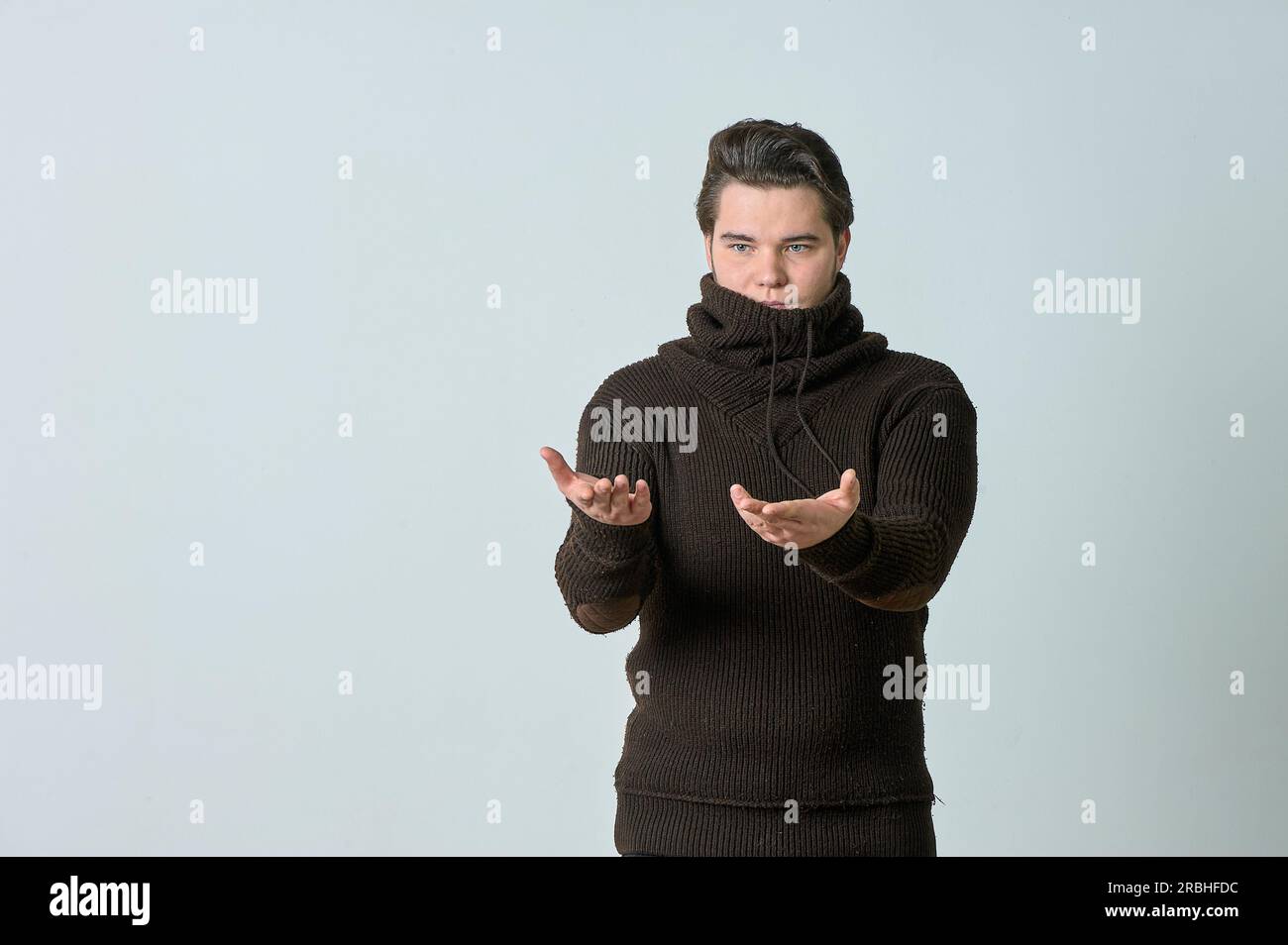 A man on a gray background in a brown sweater showing emotions, shows ...