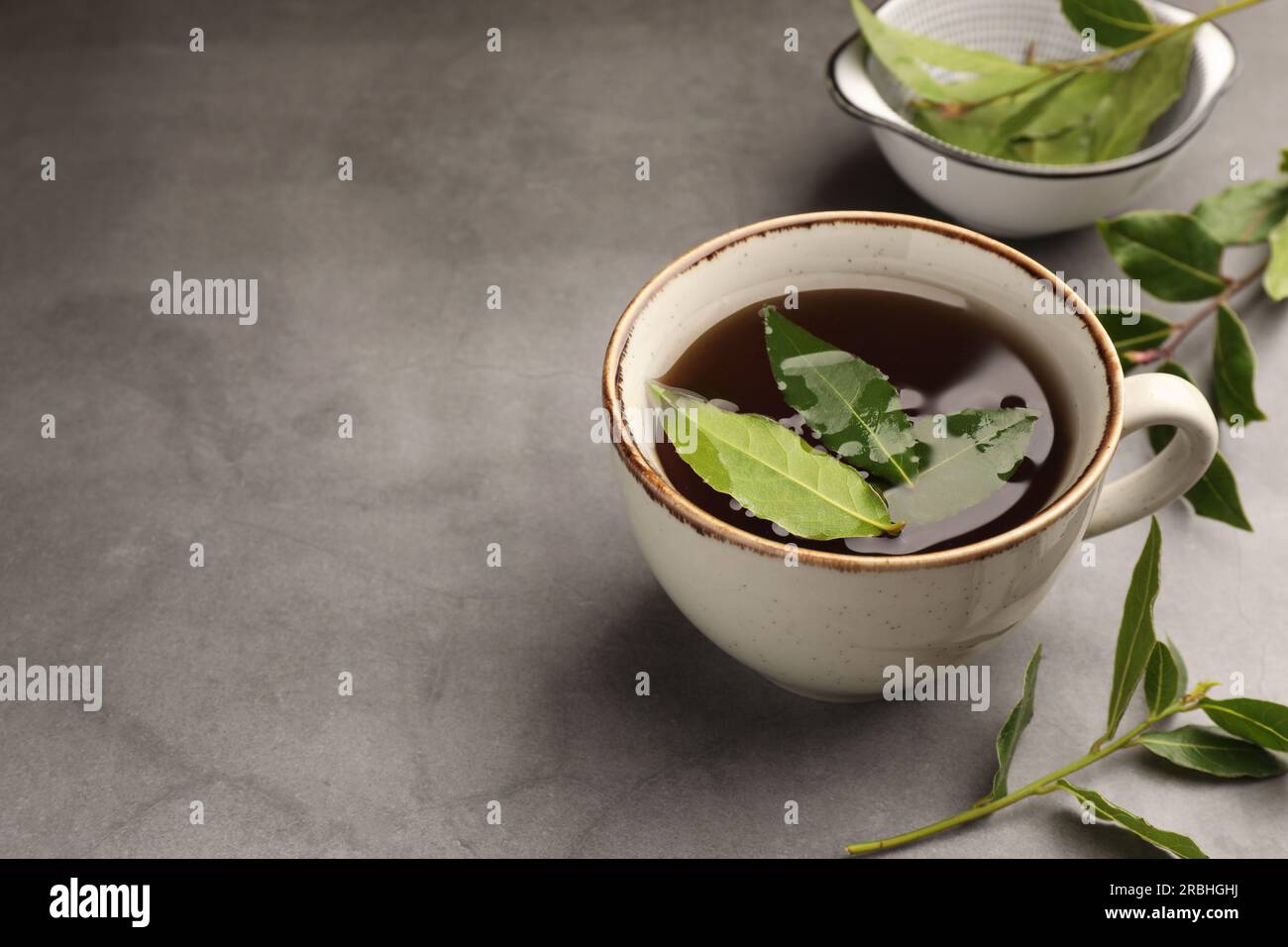 Cup of freshly brewed tea with bay leaves on grey table, space for text ...