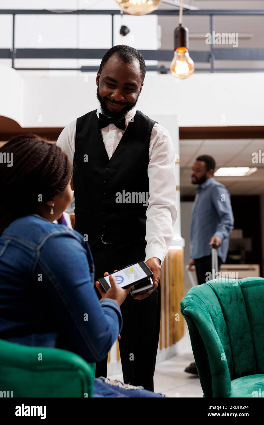 Smiling African American man waiter giving pos machine to female hotel ...