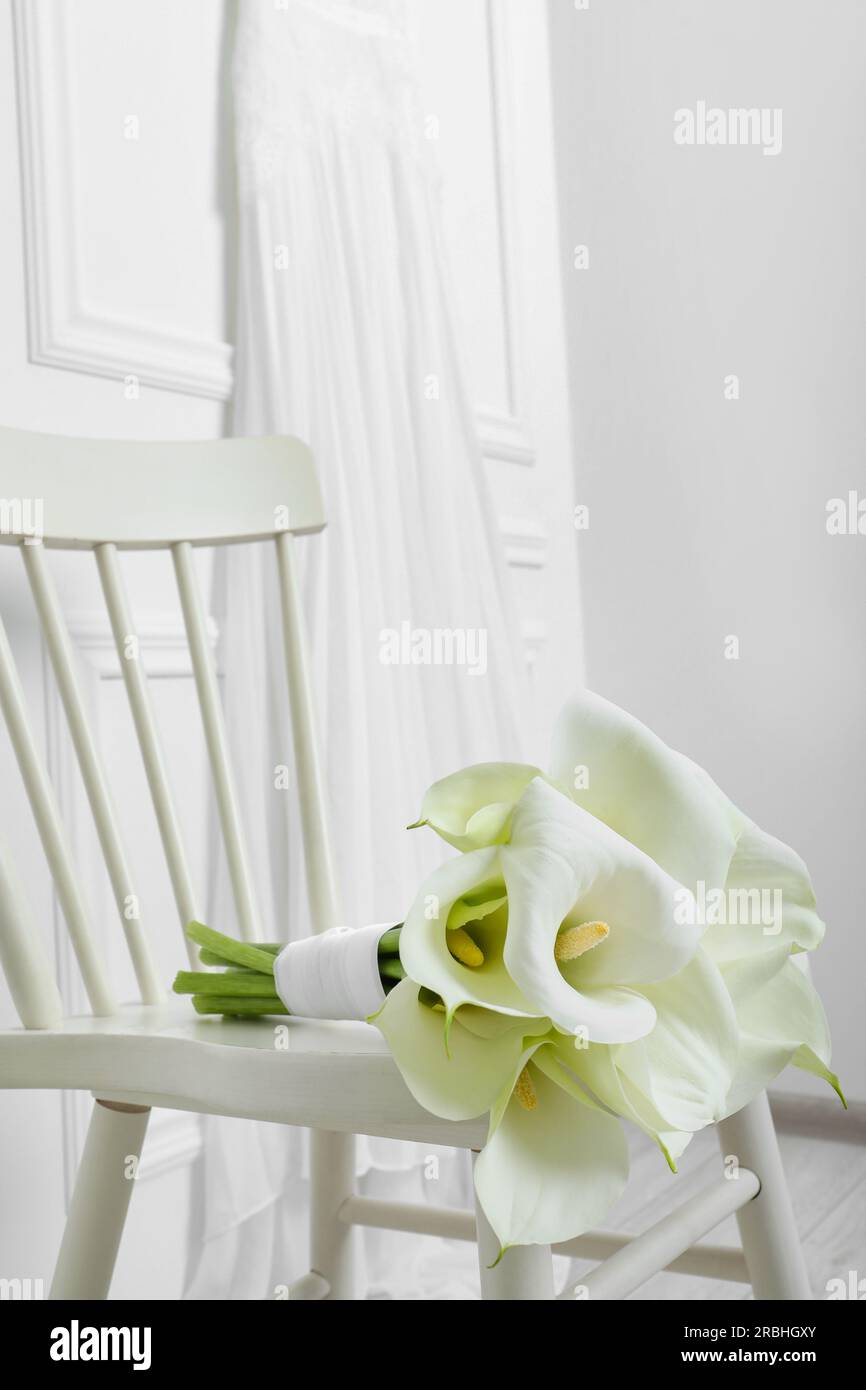 Beautiful calla lily flowers tied with ribbon on white chair indoors ...