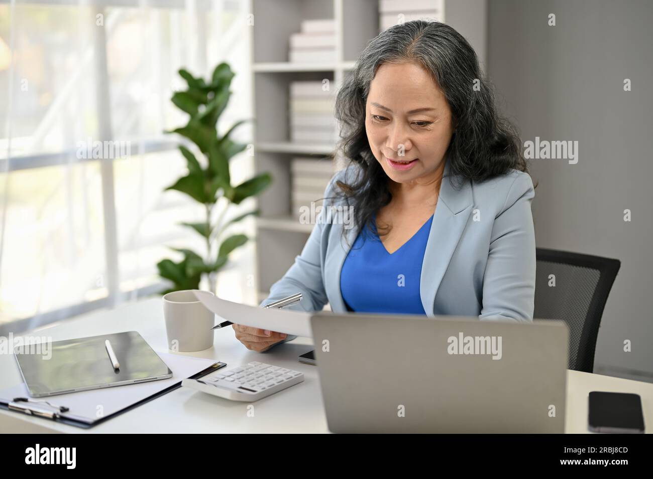 A professional and happy Asian senior female boss reading business ...