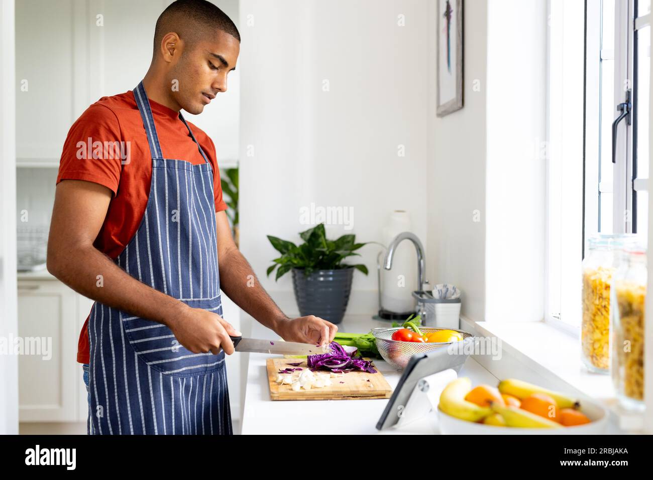 Focused biracial man chopping vegetables and using tablet in sunny ...