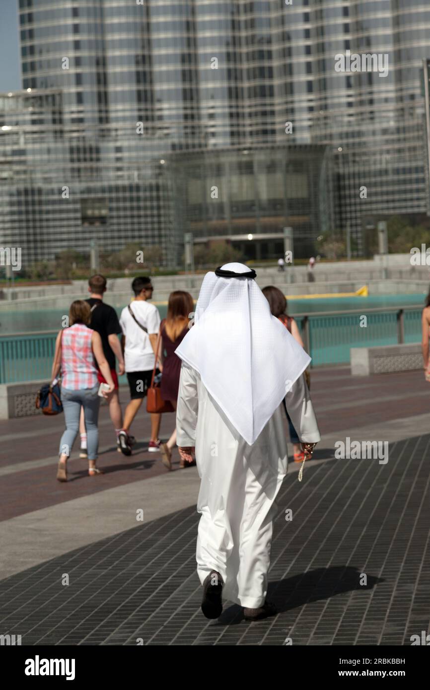 UAE, Dubai, Man in Arab dress walking along the Burj Khalifa lakeside ...
