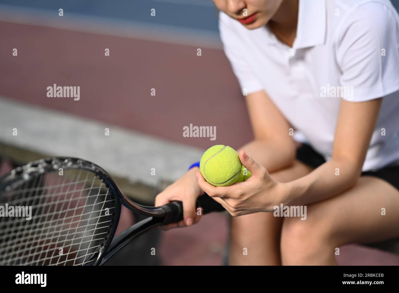Pretty young sportswoman holding ball racket sitting on the bench at ...