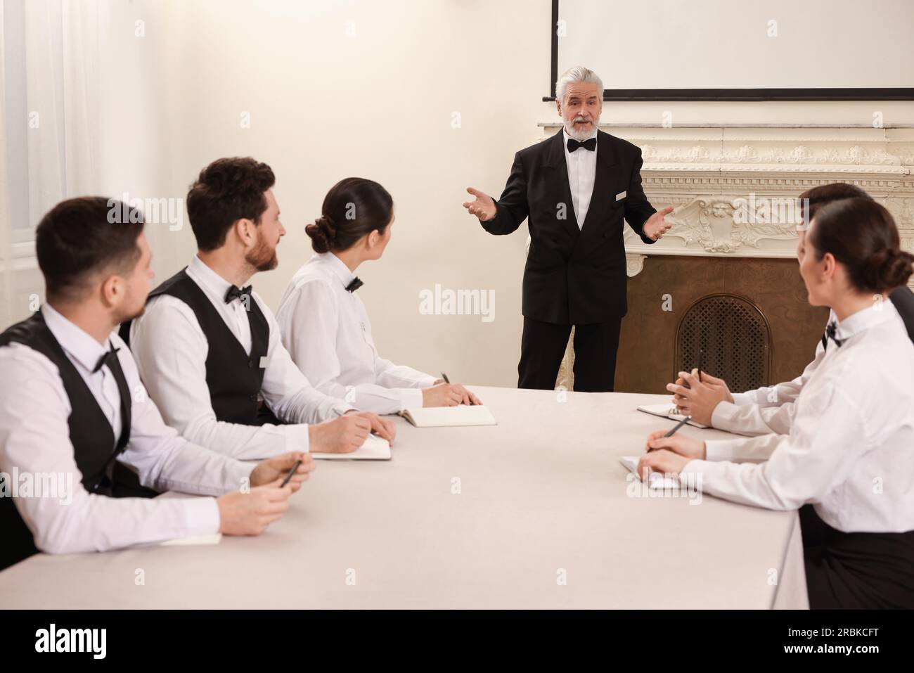 Senior man in formal suit teaching trainees indoors. Professional ...