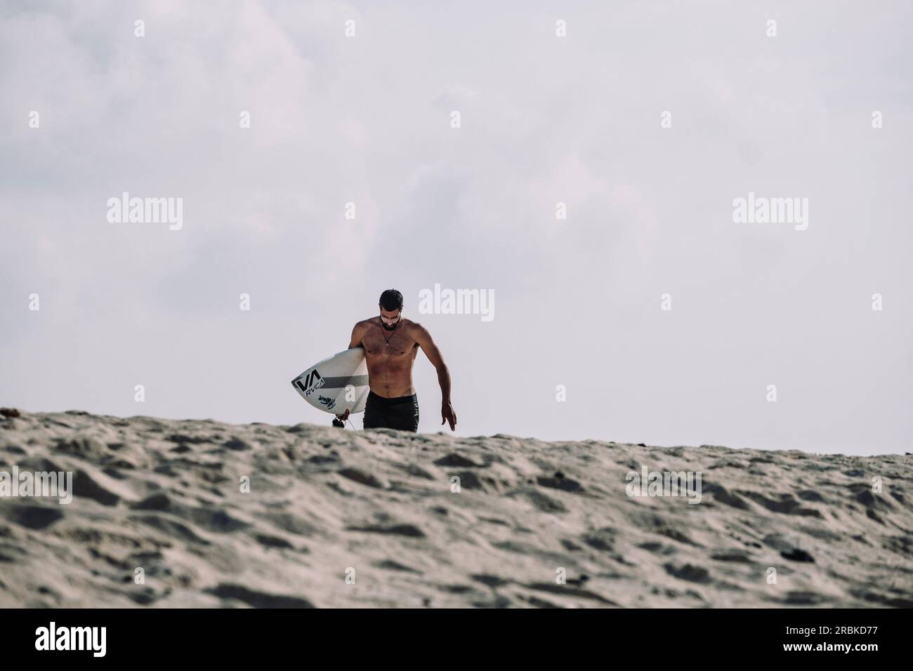 Pulled back view of surfer walking on sand Stock Photo - Alamy
