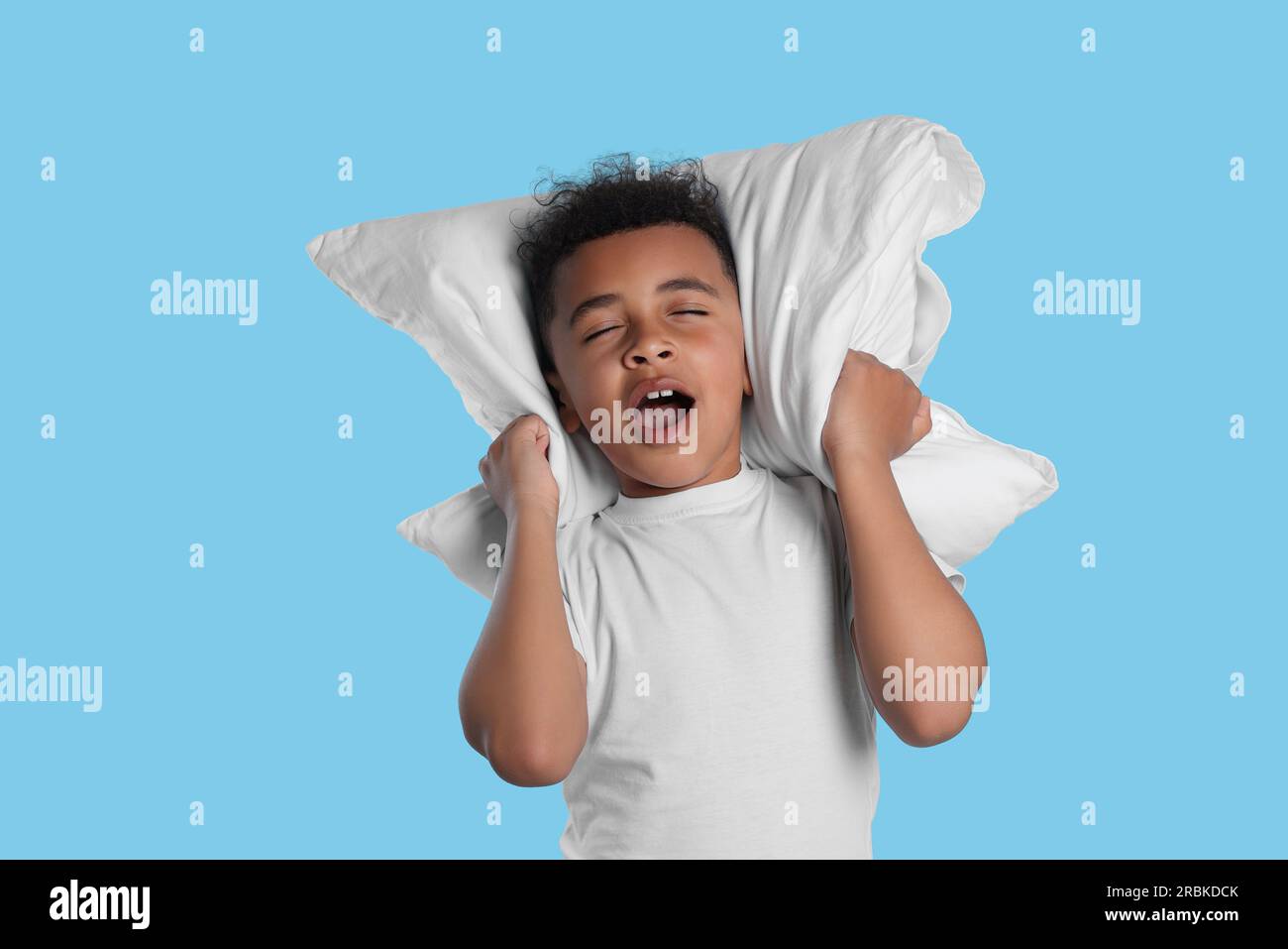 Boy covering his ears with pillow on light blue background. Insomnia ...