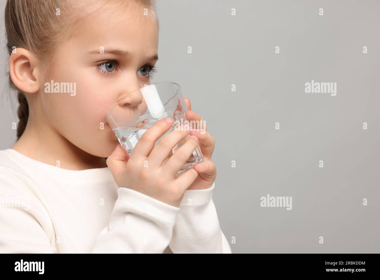 Cute little girl drinking fresh water from glass on light grey background, space for text Stock ...