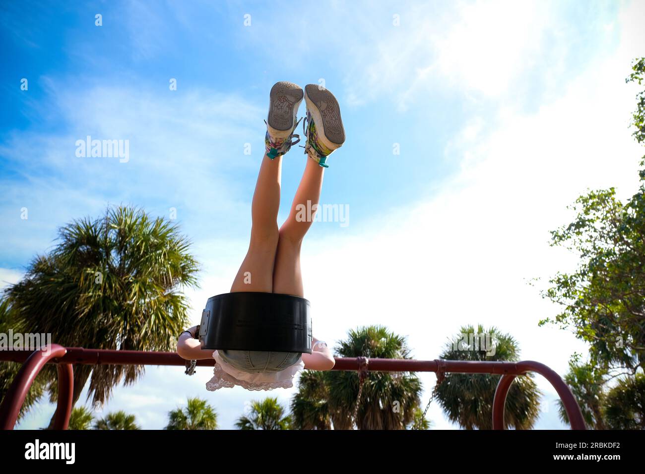 view from below of girl on swing legs in air against blue sky at park ...
