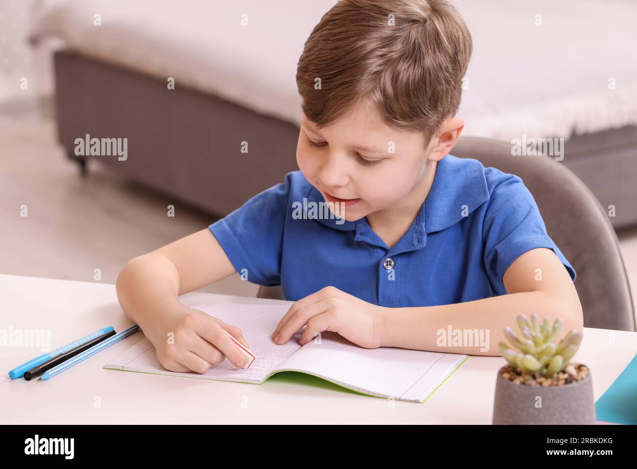 Little boy erasing mistake in his notebook at white desk indoors Stock ...