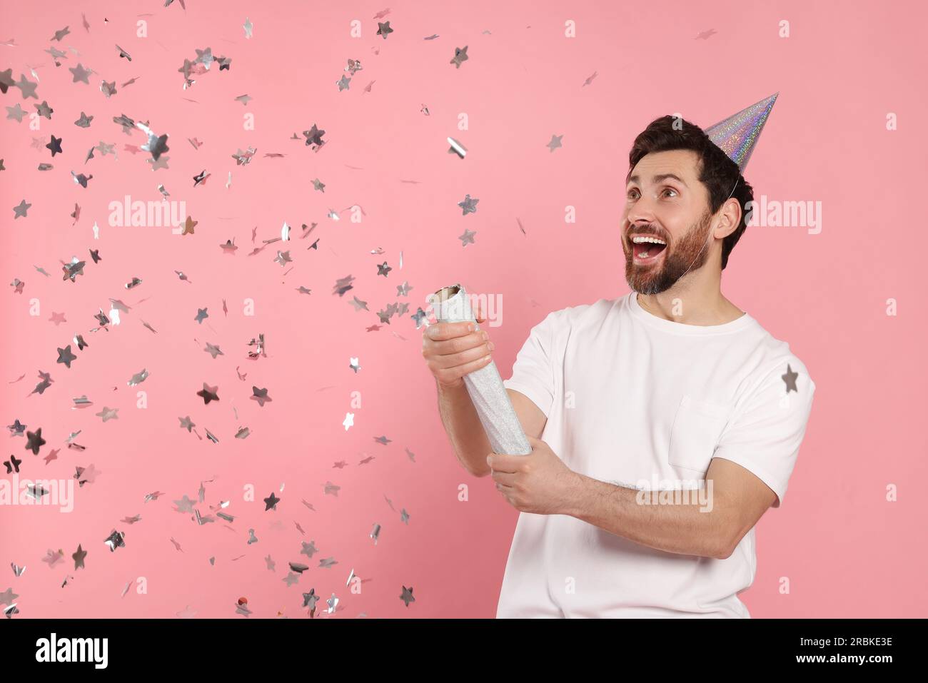 Emotional man blowing up party popper on pink background Stock Photo ...