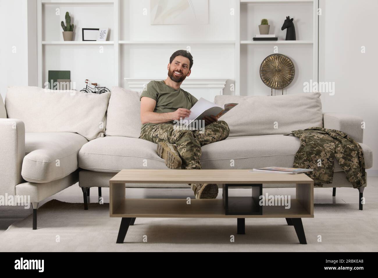 Happy soldier reading magazine on sofa in living room. Military service ...