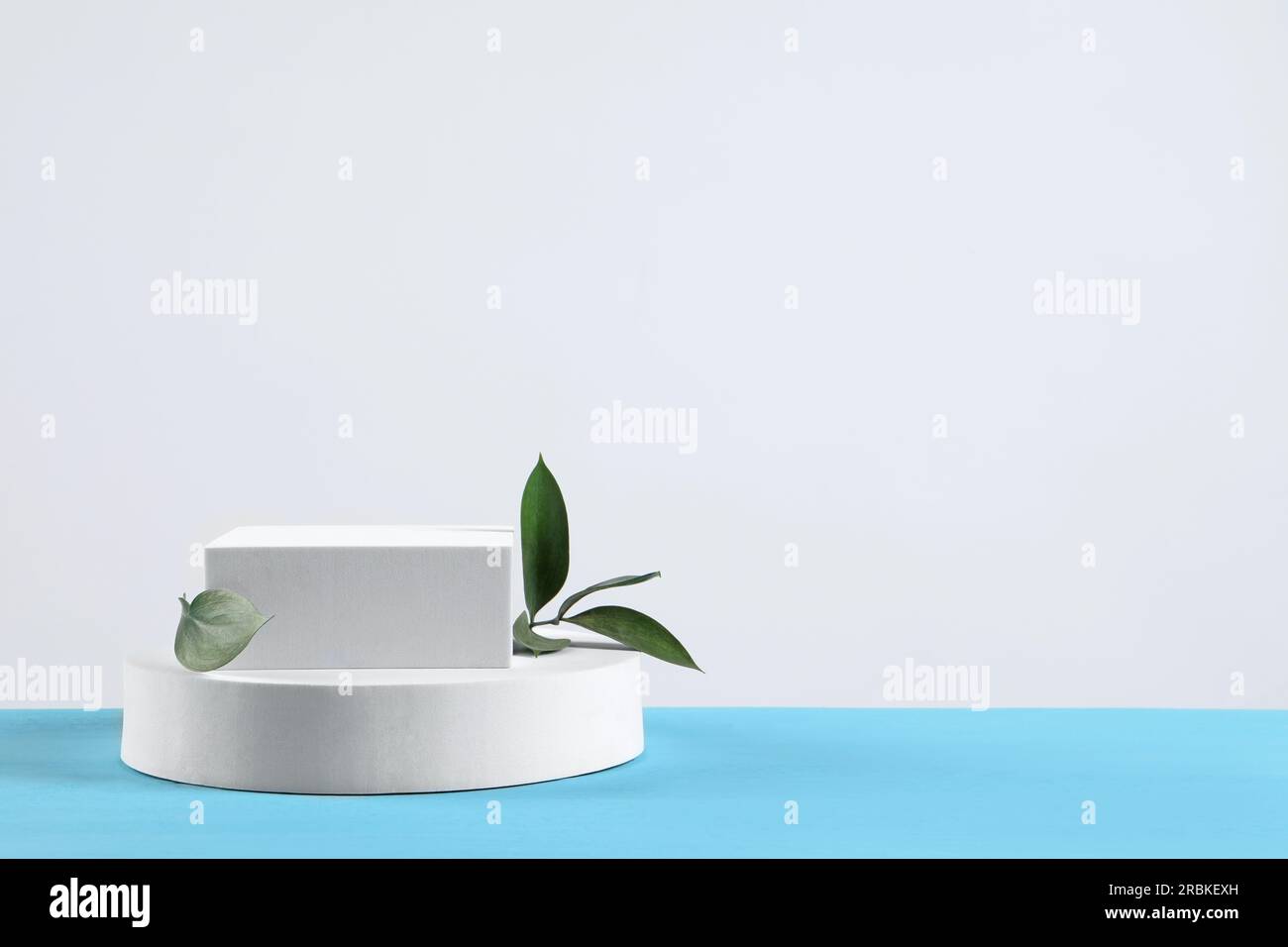 Podium with green leaves on light blue wooden table. Space for text ...