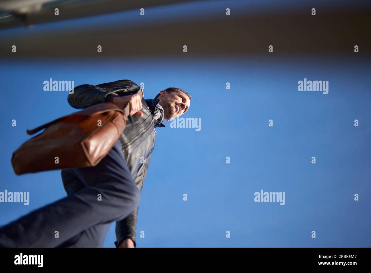 Low angle of a business man carrying a leather bag walking in sunshine ...