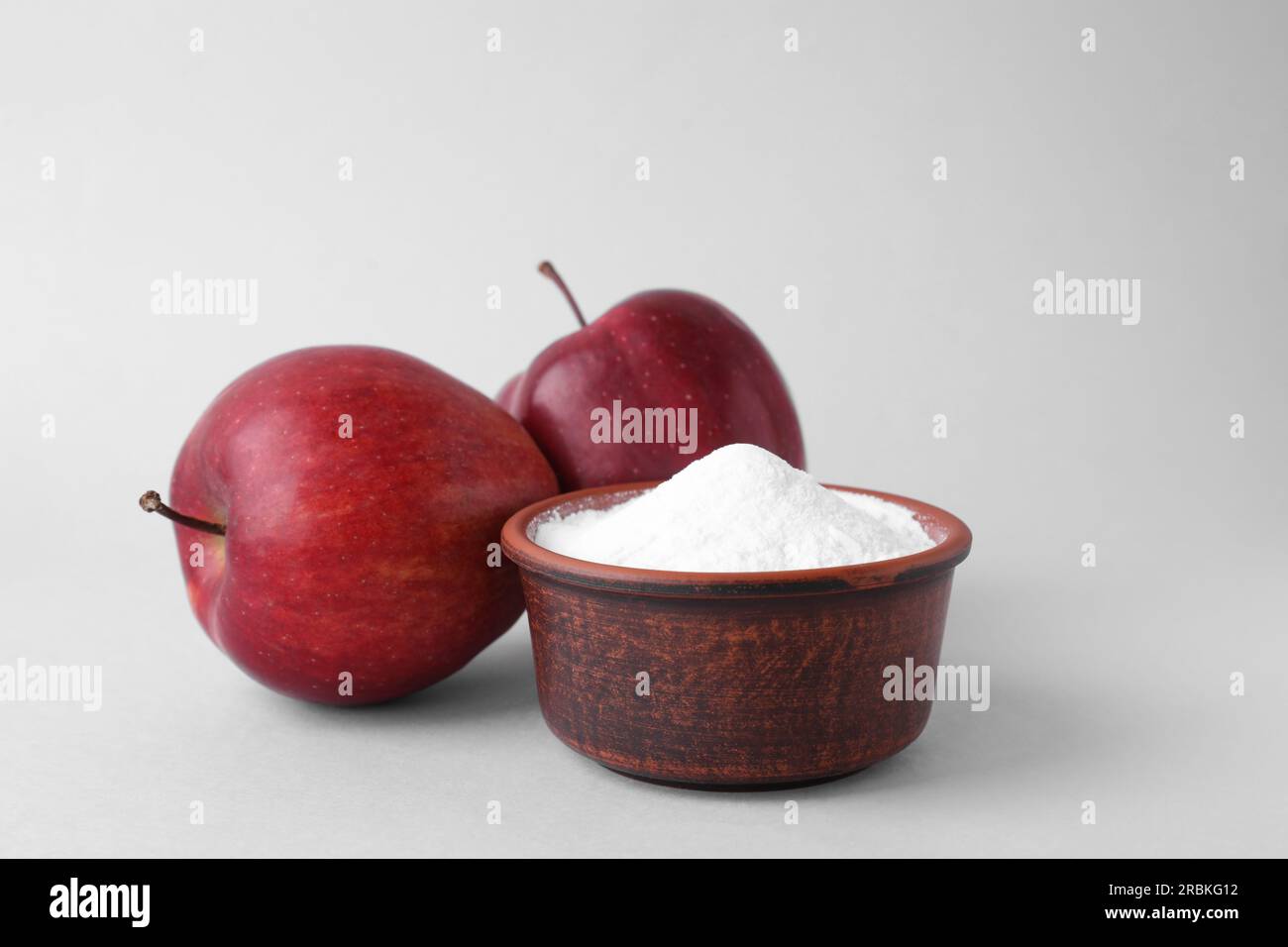 Bowl with sweet fructose powder and ripe apples on white background ...
