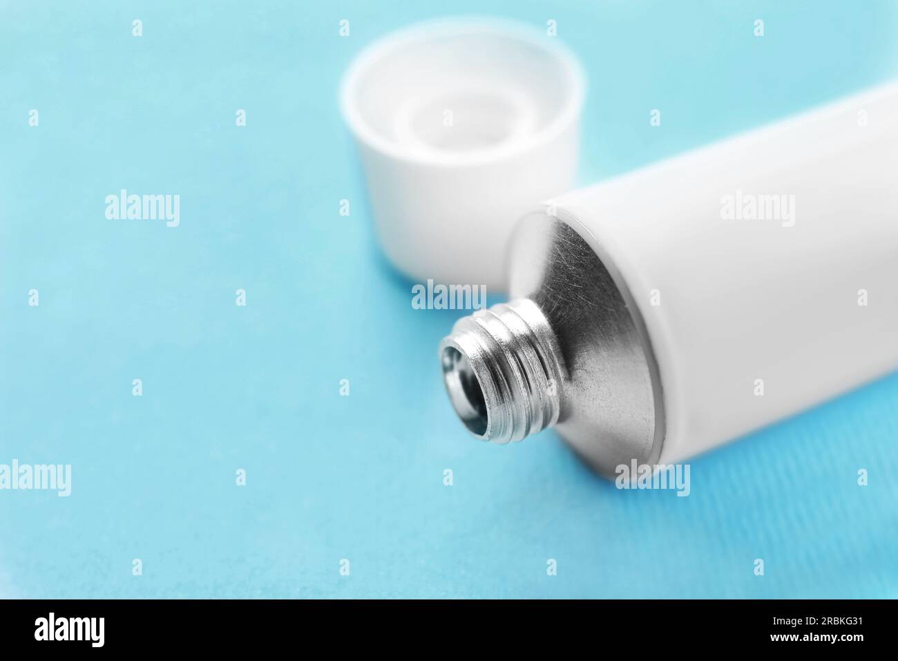 Open tube of ointment on light blue background, closeup. Space for text ...