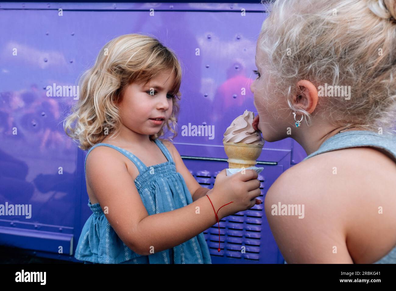 Happy pair of sisters sharing and licking ice cream cone Stock Photo - Alamy