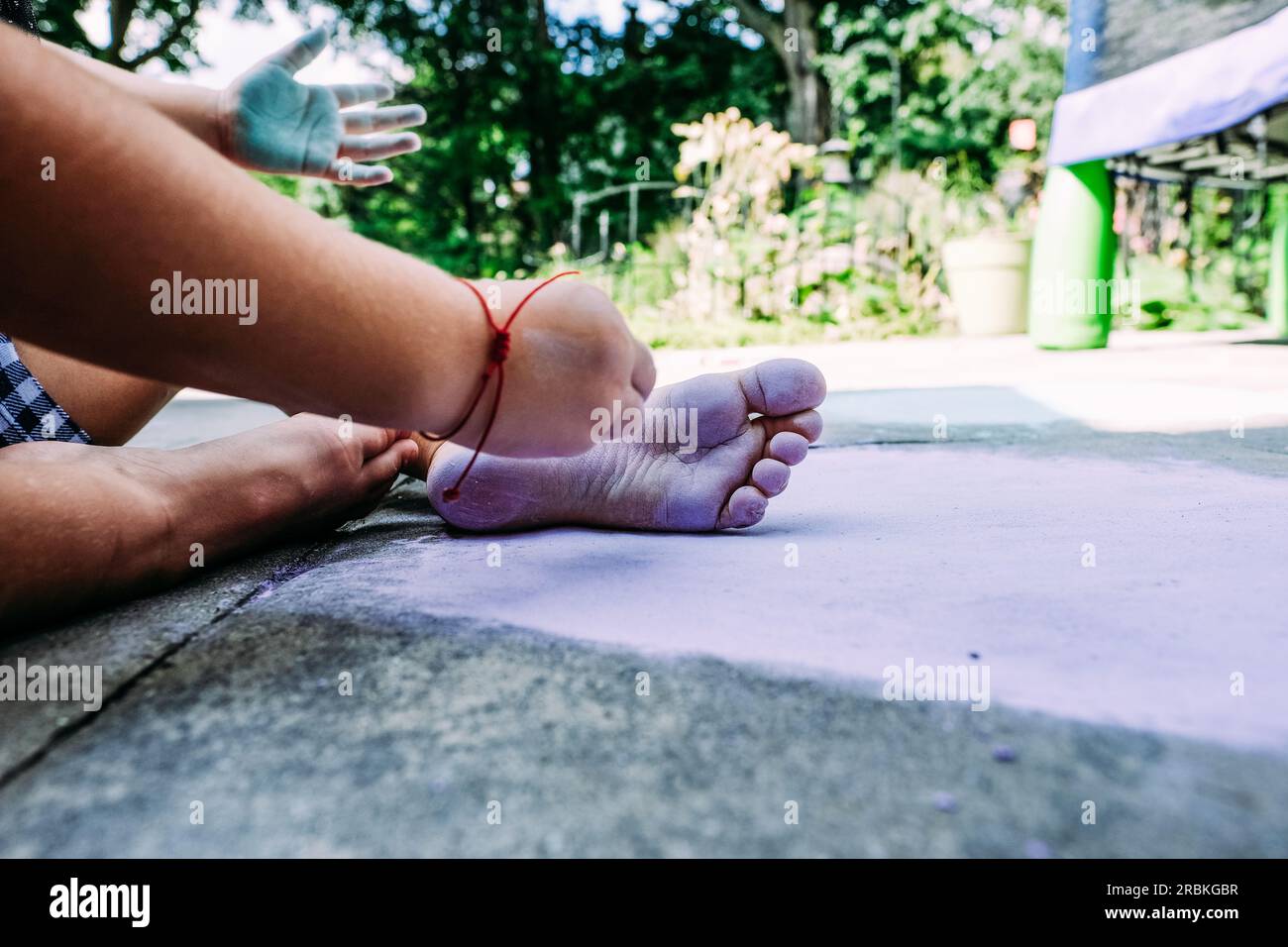 child playing outside with chalk coloring bottoms of feet in sunlight ...