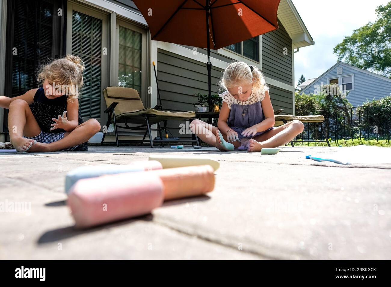 two girls playing with chalk outside in sunlight on patio Stock Photo ...