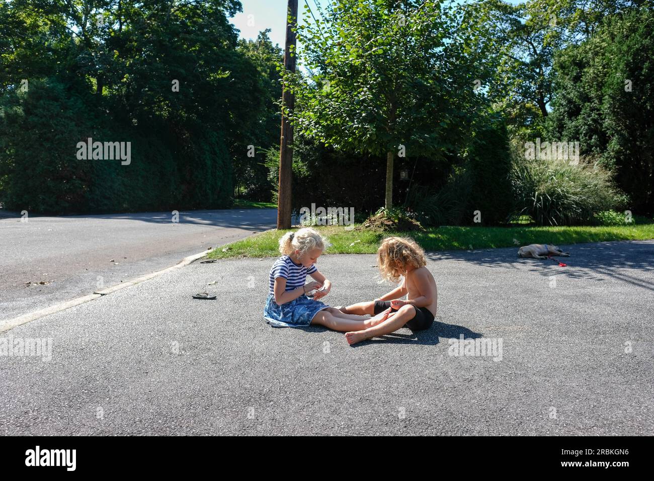 two children sitting on driveway playing in the sunlight Stock Photo ...