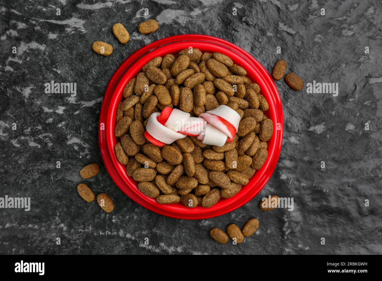 Dry dog food and treat (knotted chew bone) on black textured background ...