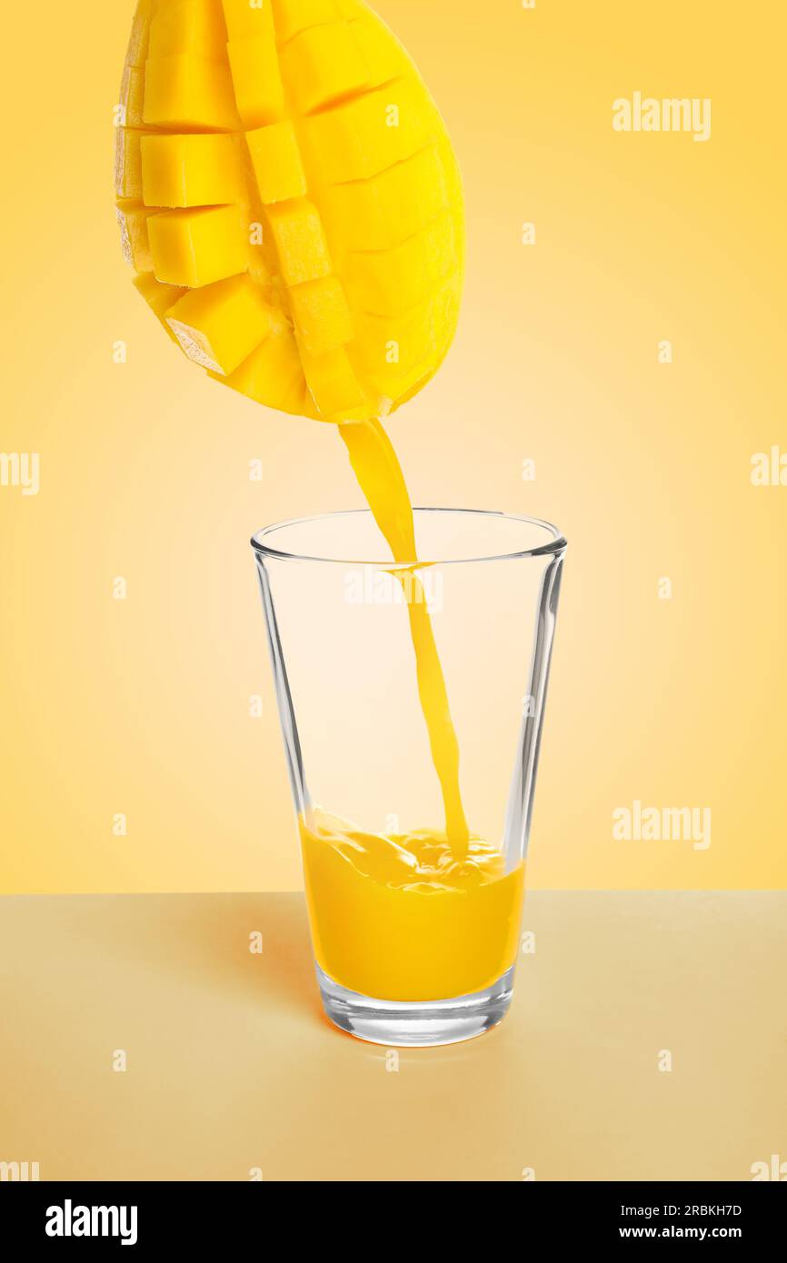 Making mango fresh. Juice pouring from mango into glass on pale yellow ...