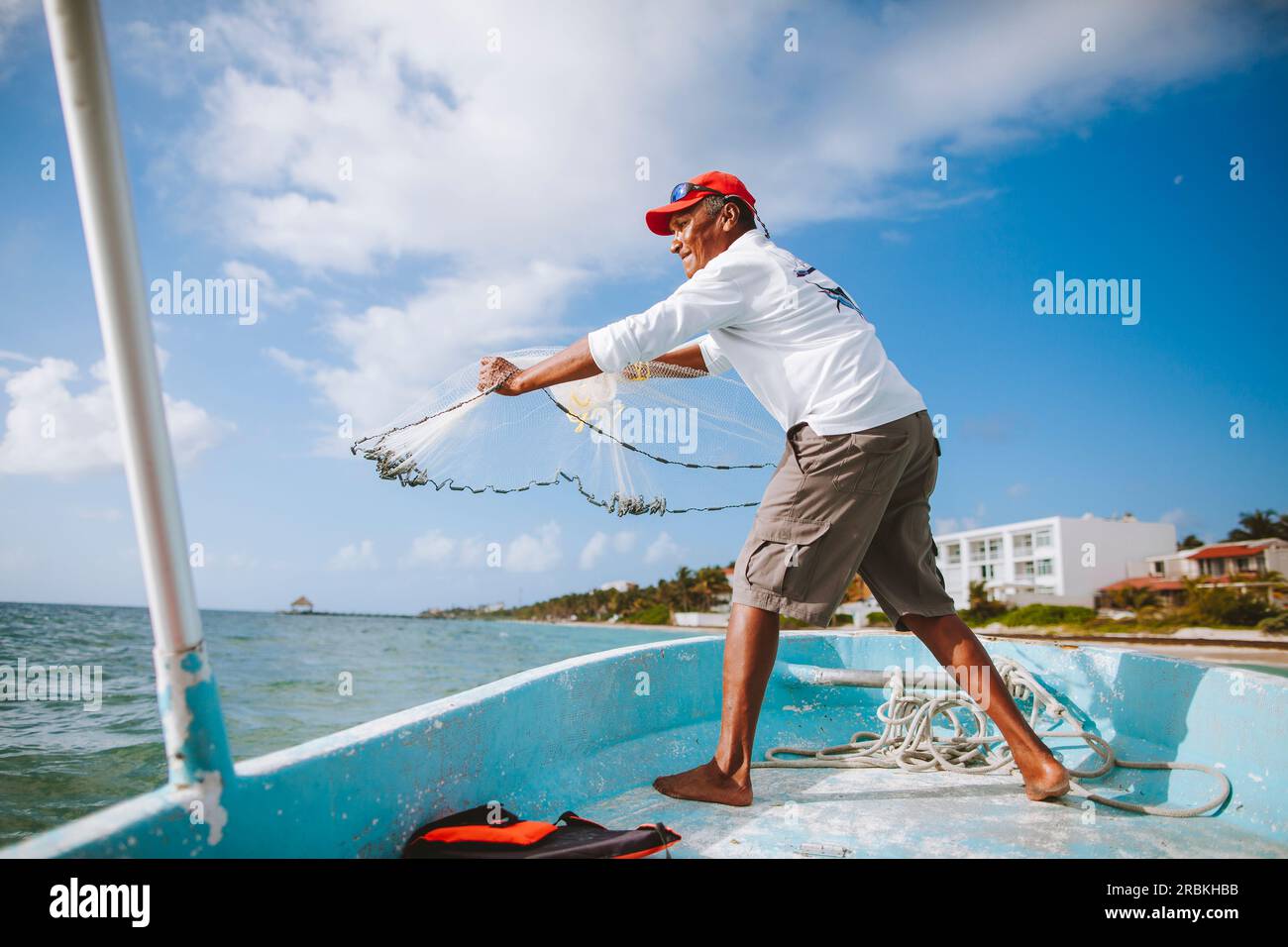 A deep sea fisher casts a net off the side of a boat near shore Stock ...