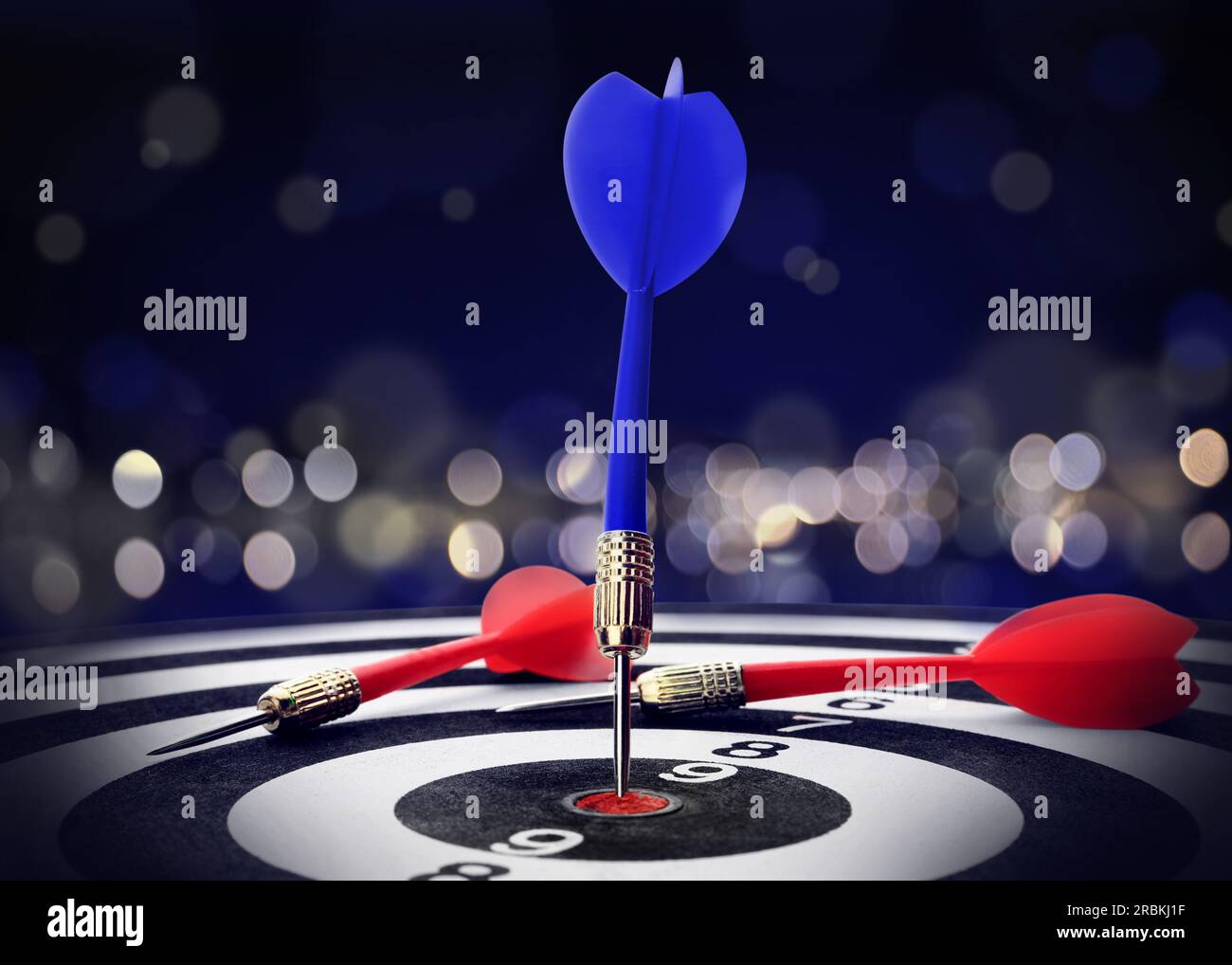 Dart board with blue arrow hitting target against blurred background ...