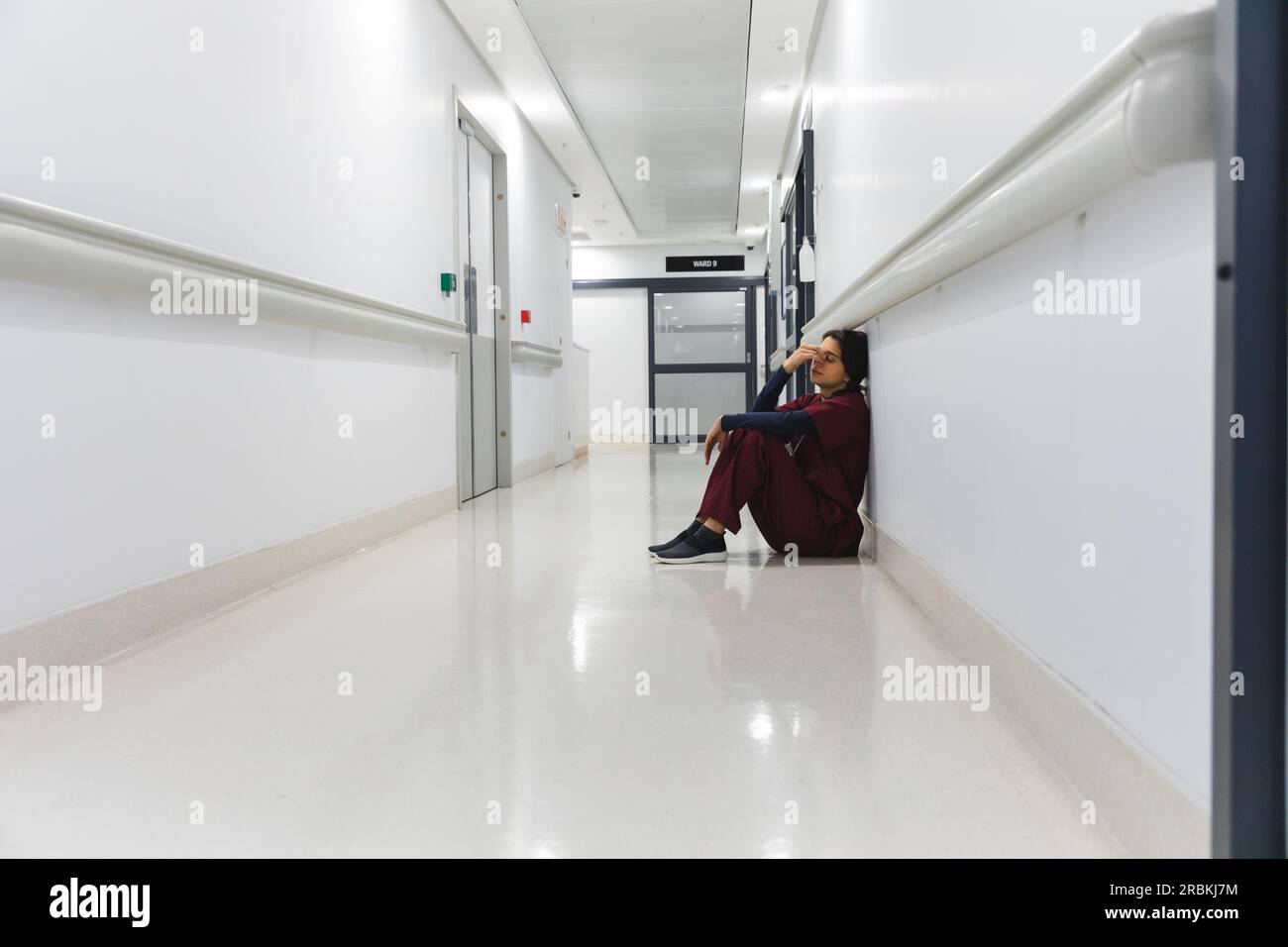 Tired caucasian female doctor wearing scrubs, sitting on floor in ...