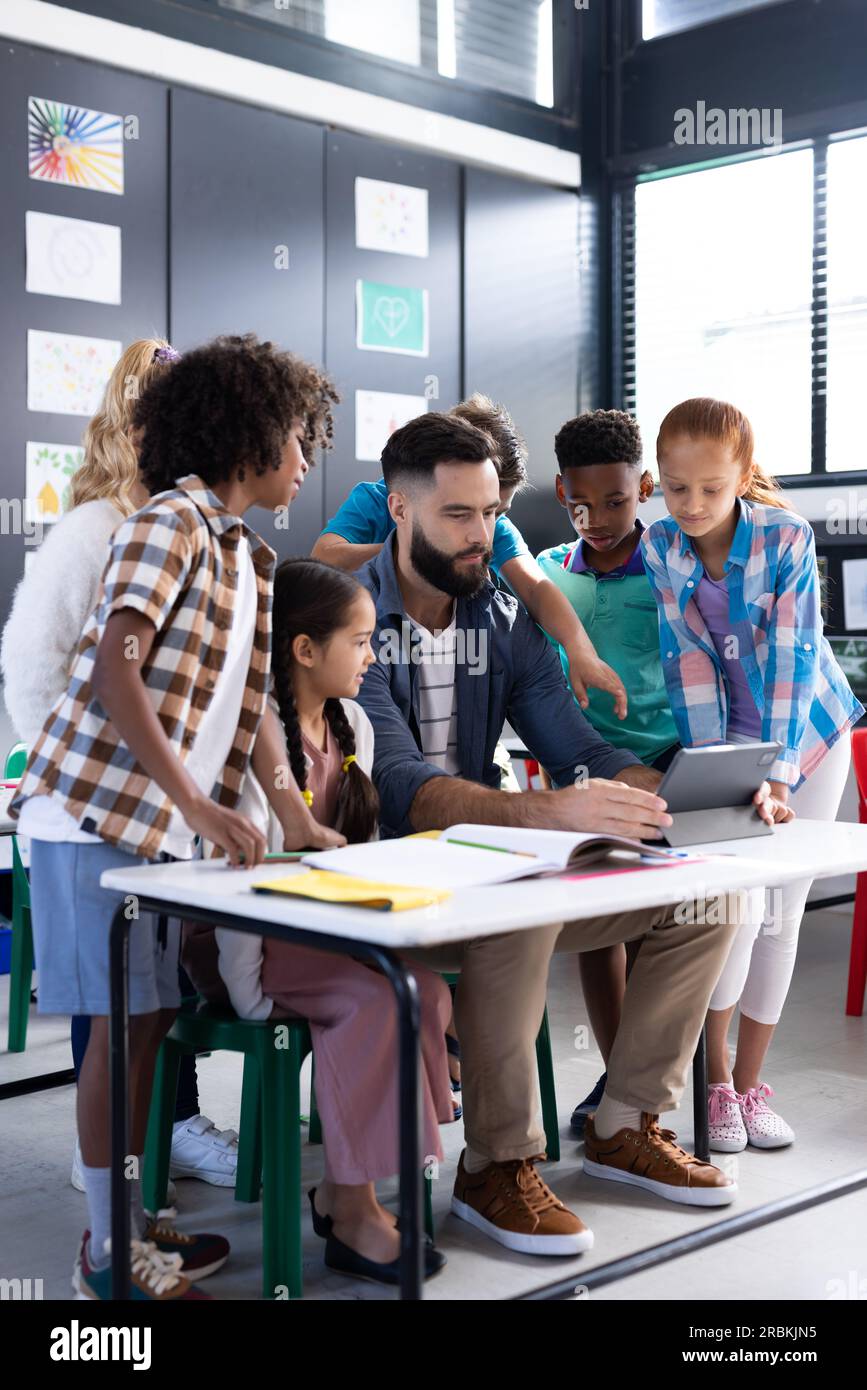 Vertical of diverse schoolchildren and male teacher using tablet ...