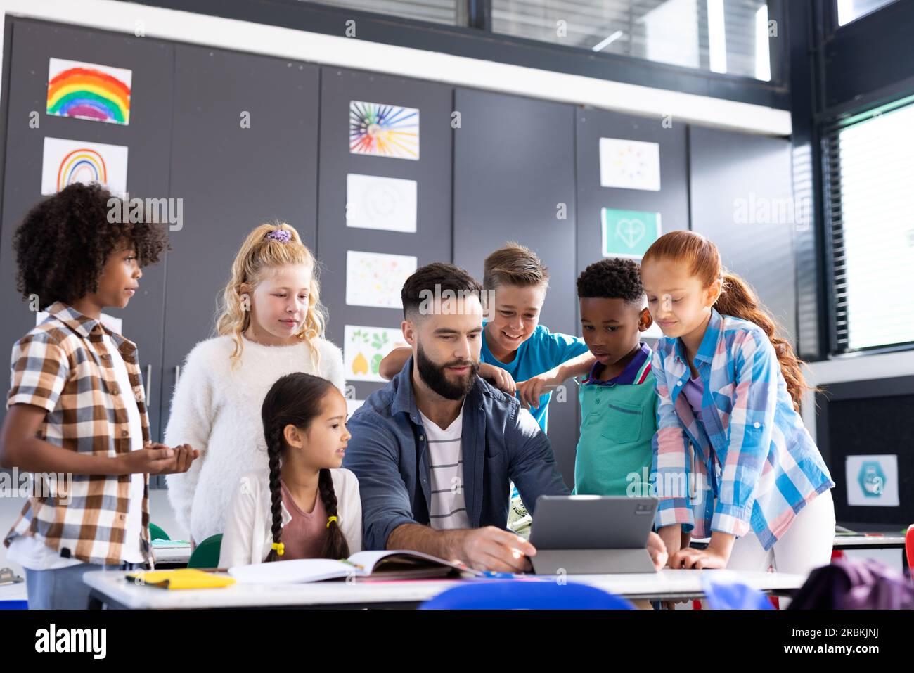 Diverse elementary schoolchildren and male teacher using tablet ...