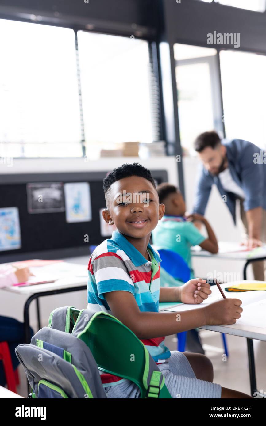 Vertical portrait of smiling african american schoolboy at desk in ...