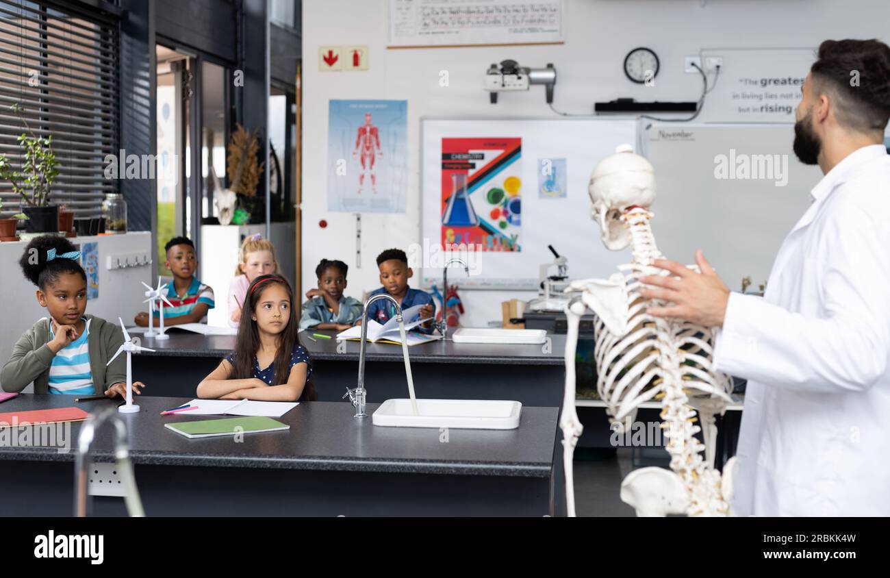 Diverse male teacher and elementary schoolchildren studying skeleton in ...