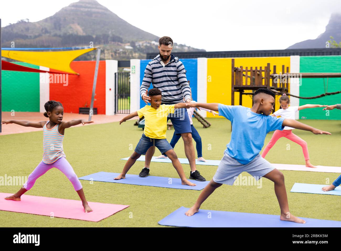 Diverse male teacher and elementary schoolchildren learning yoga in ...