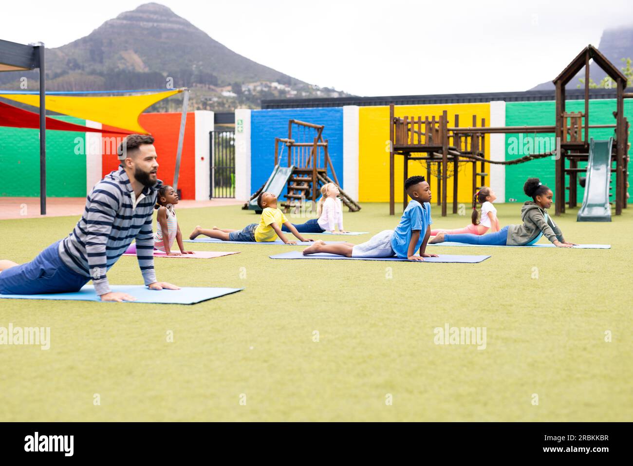 Diverse male teacher and elementary schoolchildren practicing yoga in ...