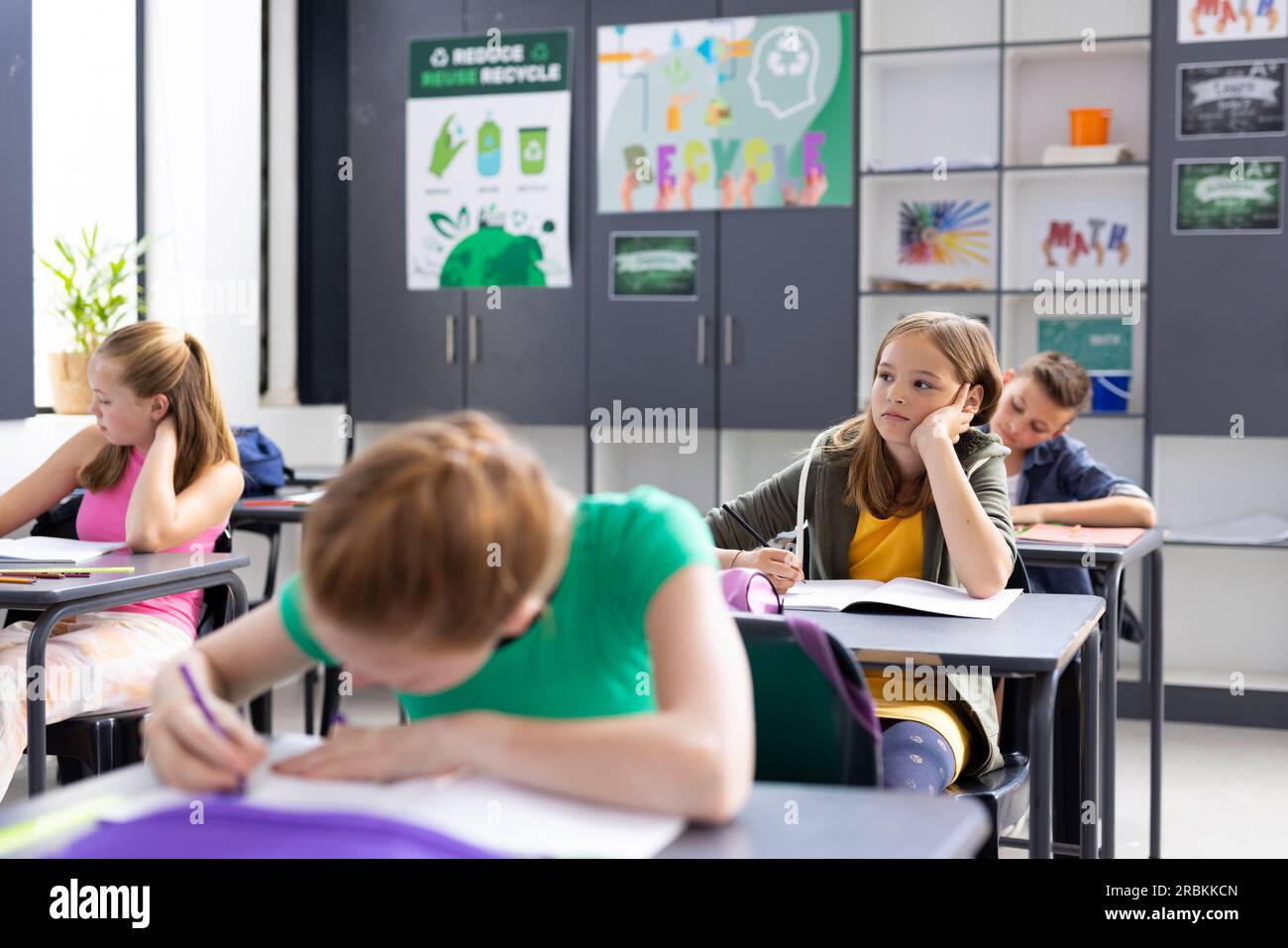 Caucasian schoolgirl sitting at desk thinking in class with classmates ...
