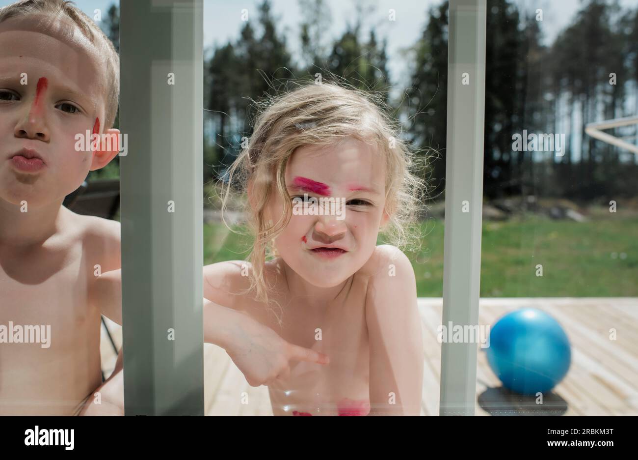 young girl making faces through a window with paint on her face Stock ...
