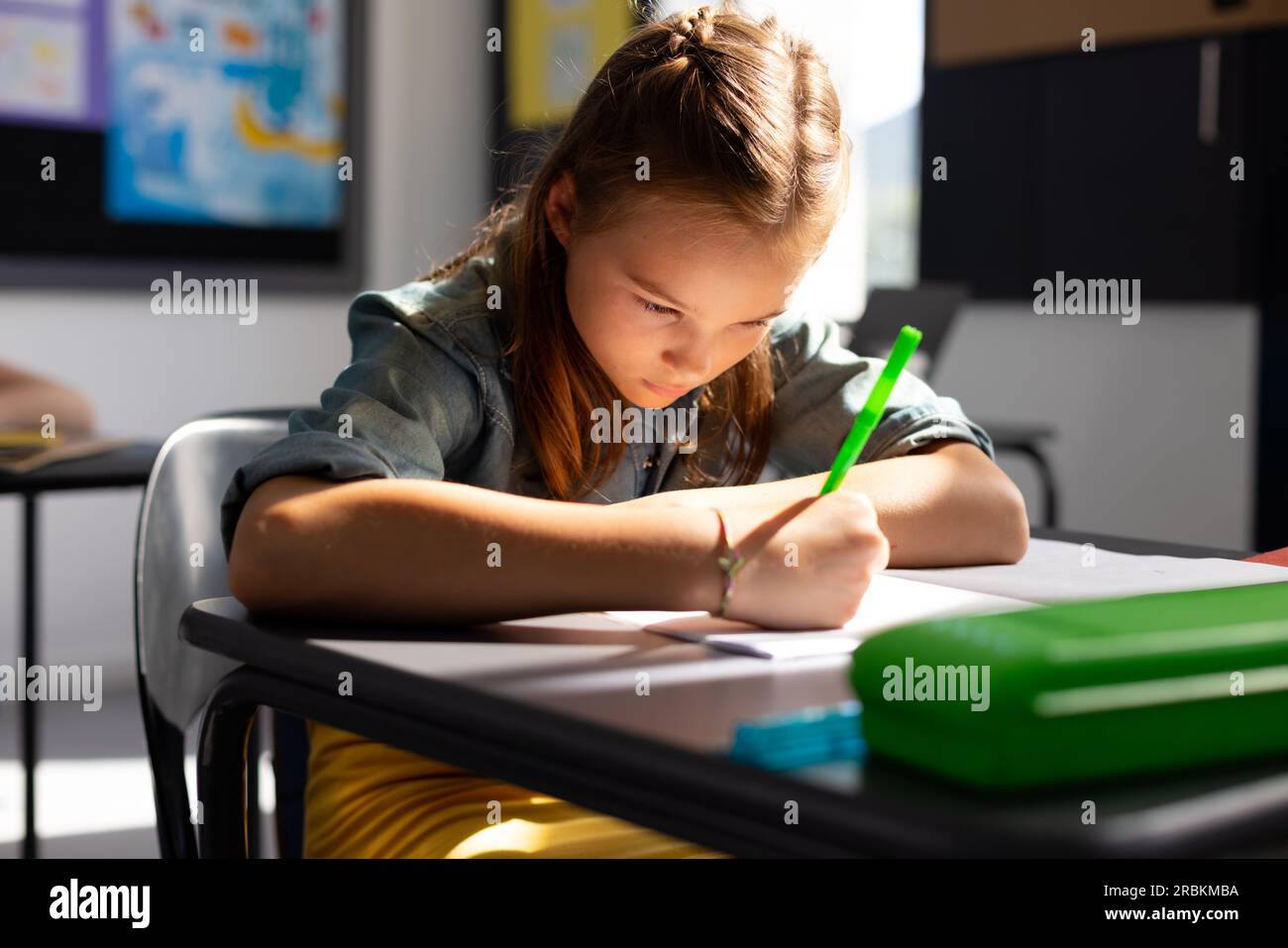 Caucasian schoolgirl sitting at desk and taking notes in school ...