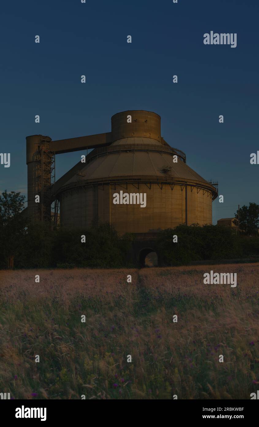 A cement factory silo seen next to a meadow of wildlife and wildflowers ...
