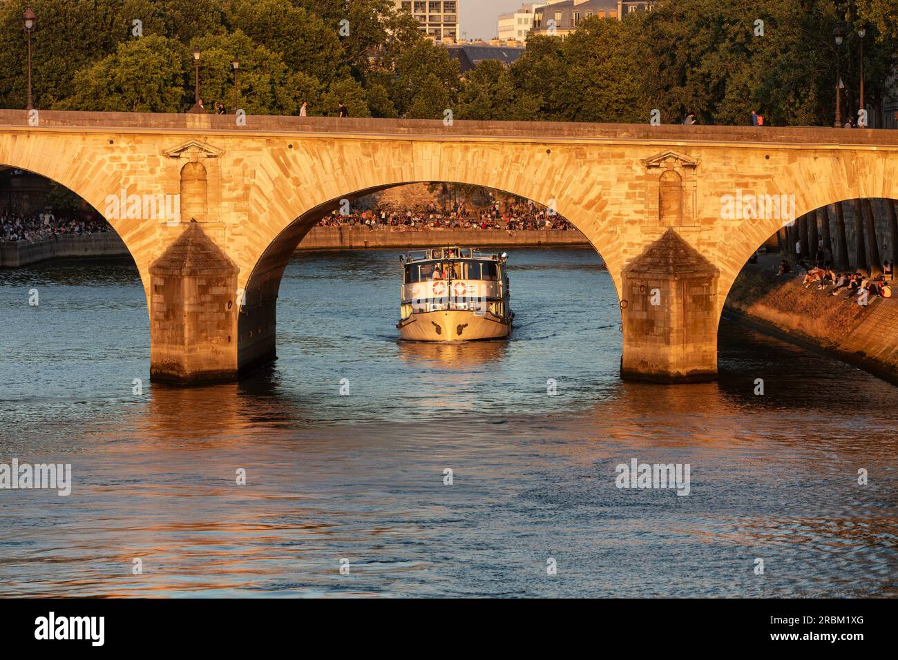 Romantic Paris. Evening light on cruise boat on River Seine passing by Pont Marie (bridge ...