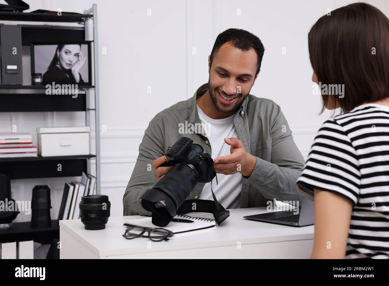 Young professional photographer showing camera to woman in modern photo ...
