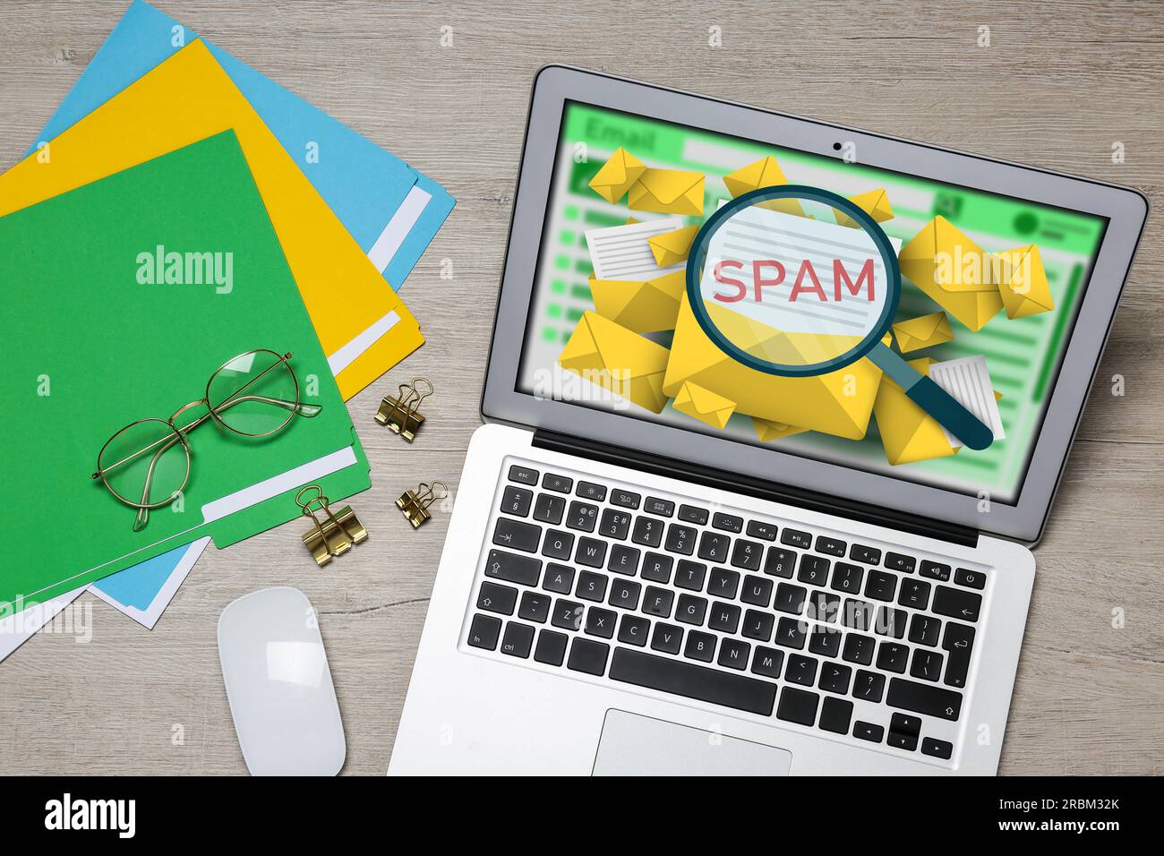 Laptop display with spam warning message in email software. Device and stationery on wooden desk ...