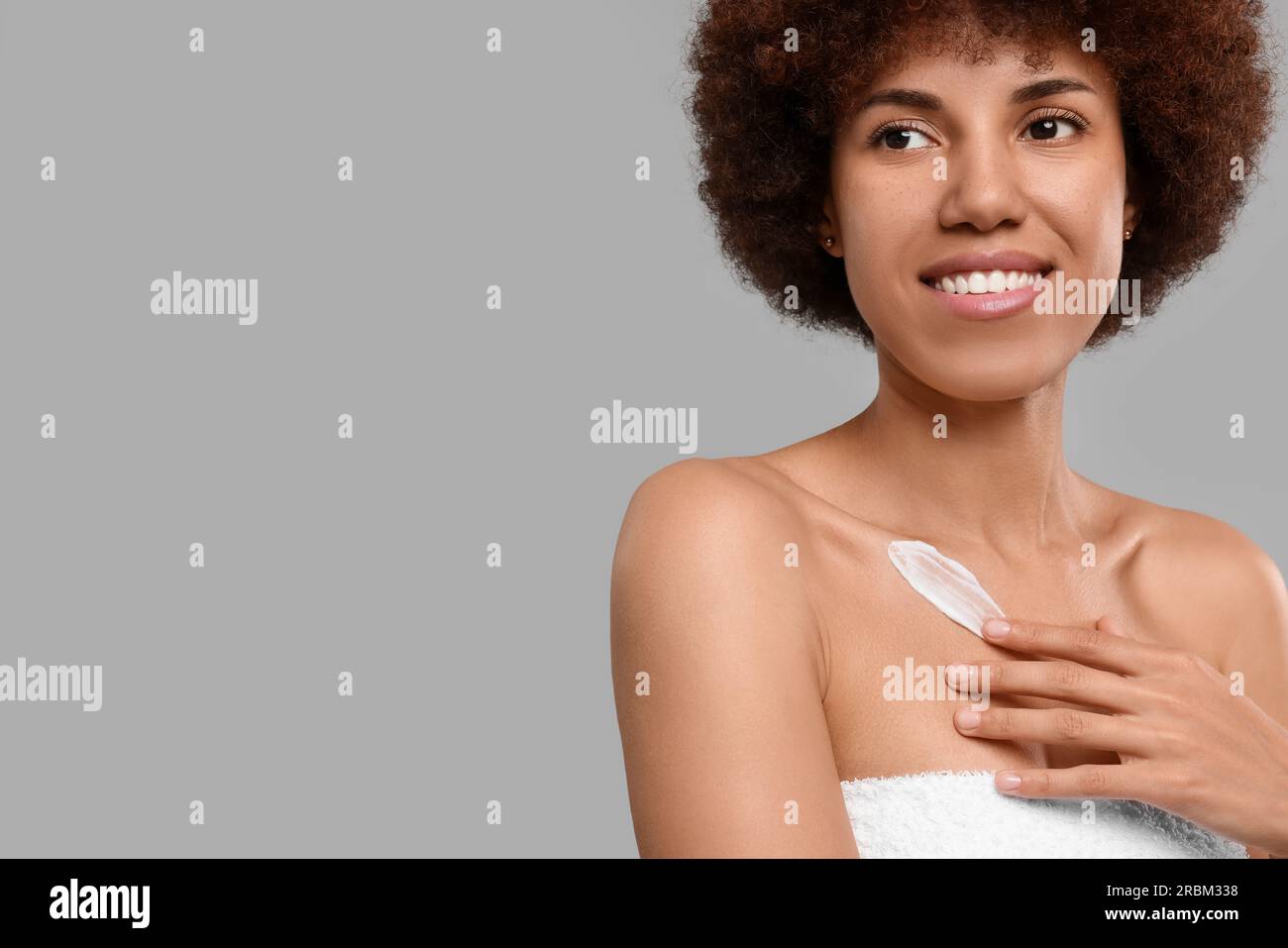 Beautiful young woman applying cream onto body on grey background ...