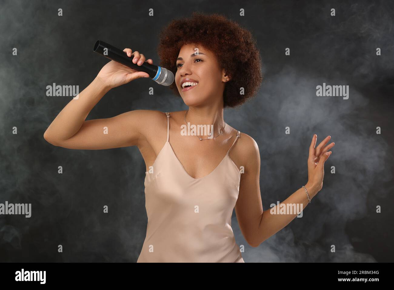 Curly young woman with microphone singing in smoke on black background ...