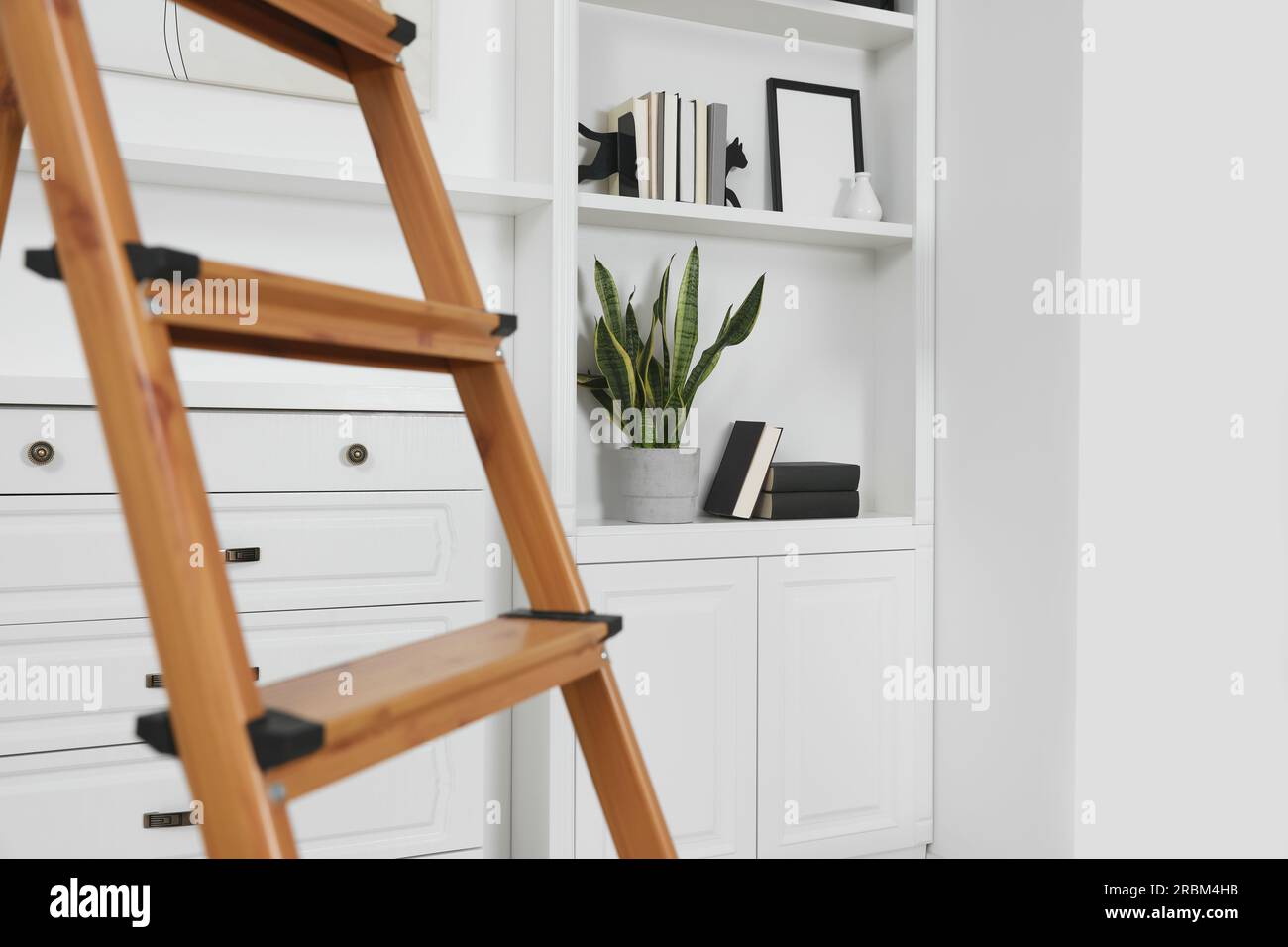 Wooden folding ladder near chest of drawers and shelf with accessories ...