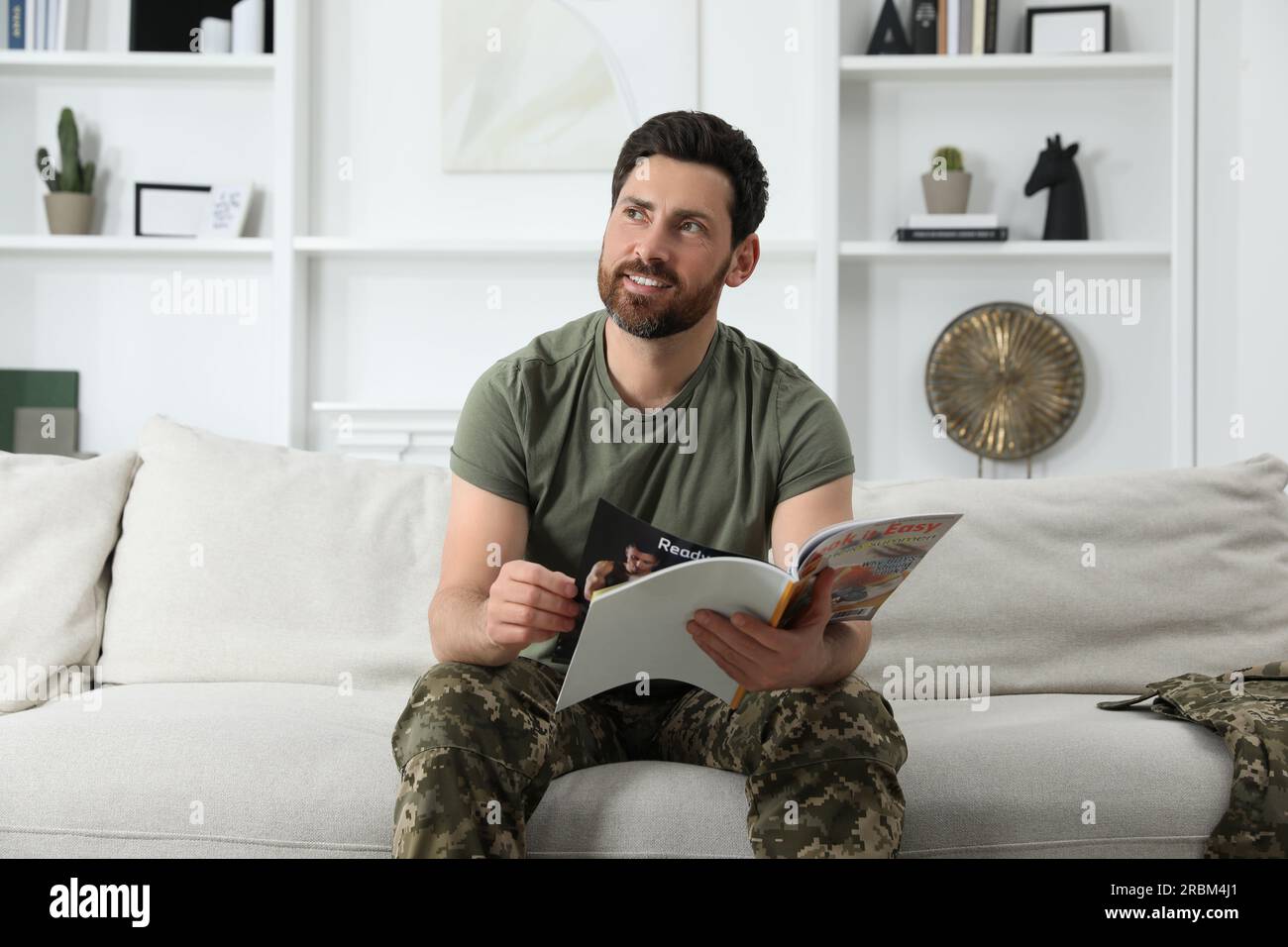 Soldier with magazine on sofa in living room. Military service Stock ...