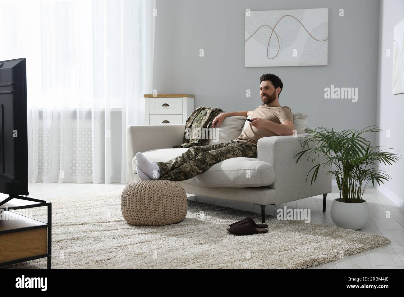 Happy soldier watching TV on sofa in living room. Military service ...