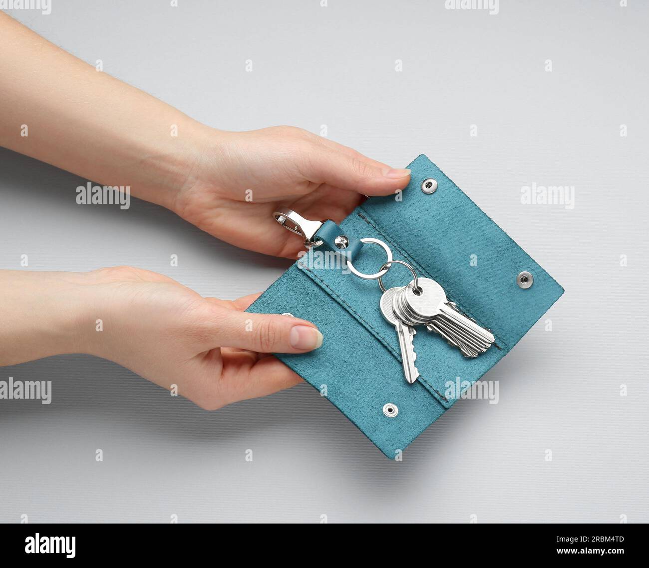 Woman holding open leather holder with keys on light grey background ...