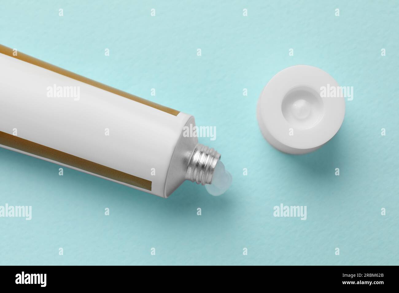 Open tube of ointment on light blue background, flat lay. Space for ...