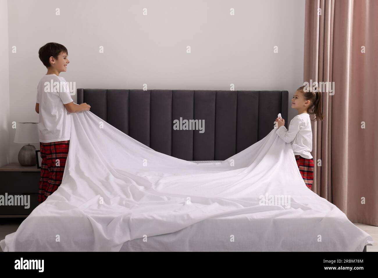 Brother and sister changing bed linens together in bedroom Stock Photo ...